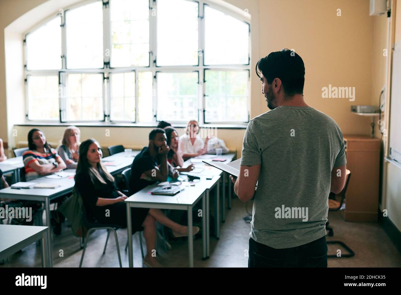Rear view of male teacher standing while teaching students in classroom ...