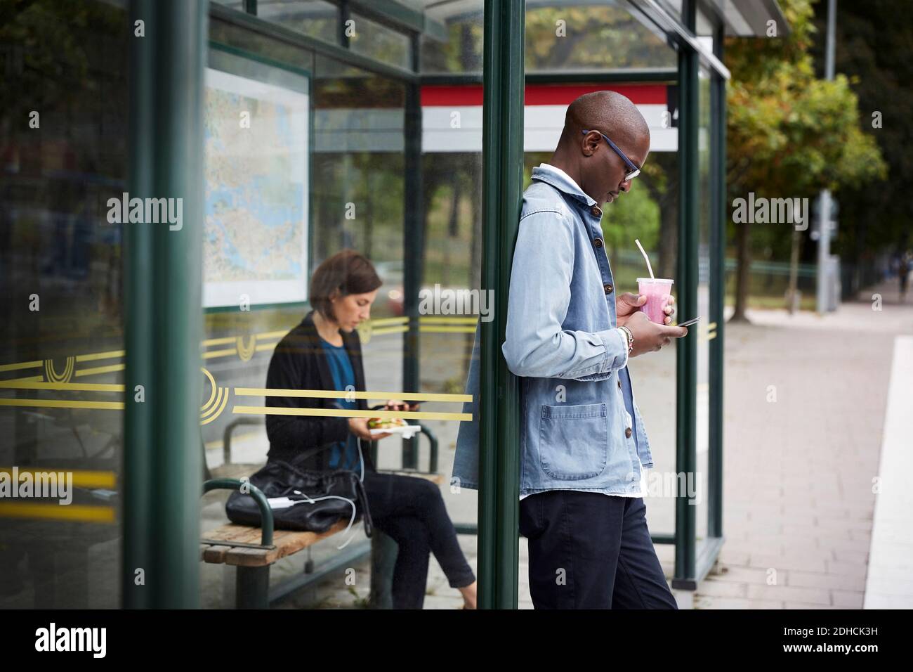 Mid adult commuters waiting at bus stop in city Stock Photo - Alamy