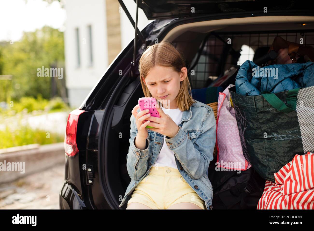 Blond girl using smart phone while sitting in electric car trunk Stock ...