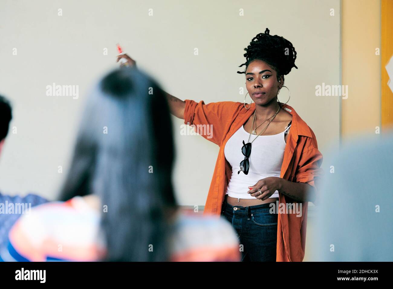 Young female teacher pointing on whiteboard while teaching students in ...