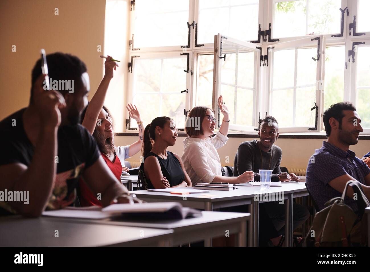 Intelligent students raising arms to answer in classroom Stock Photo ...