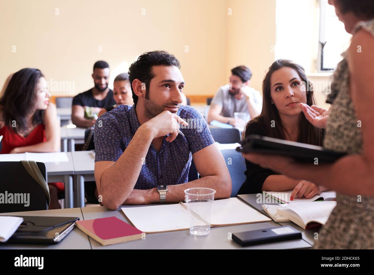 Male and female students looking at teacher explaining in classroom ...