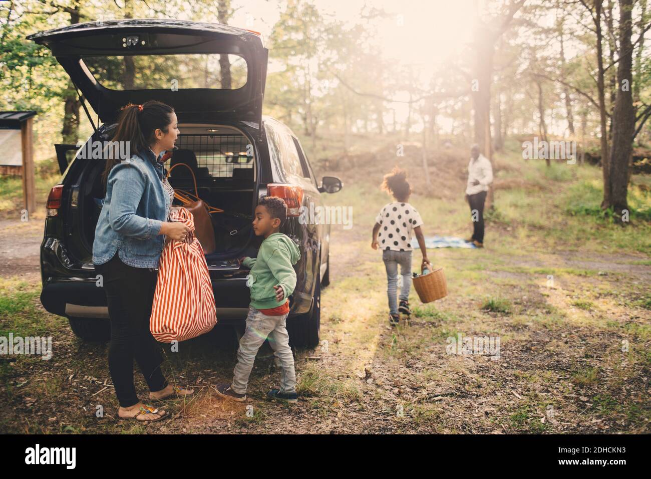 Family unloading luggage from electric car trunk at park Stock Photo ...