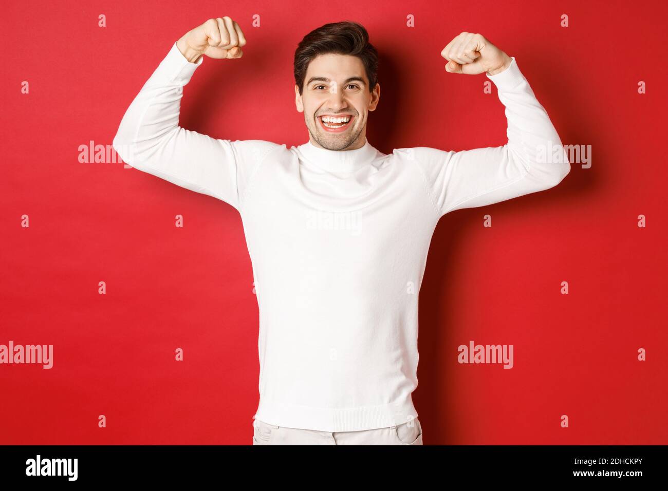 Portrait of smiling handsome man in white sweater, flexing biceps and ...