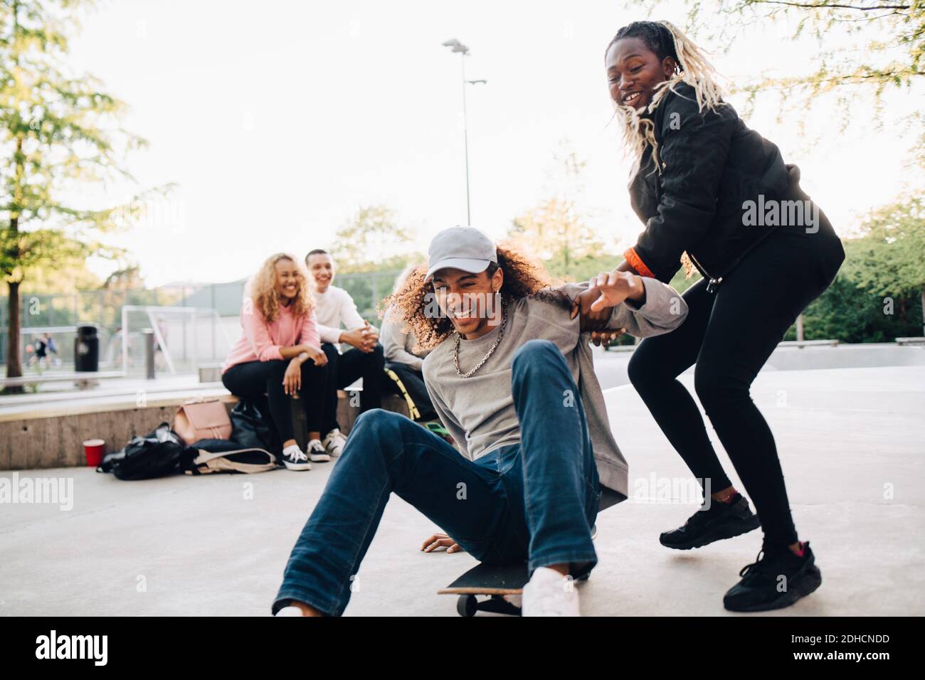 Teenage girl pushing happy man on skateboard while playing at park ...