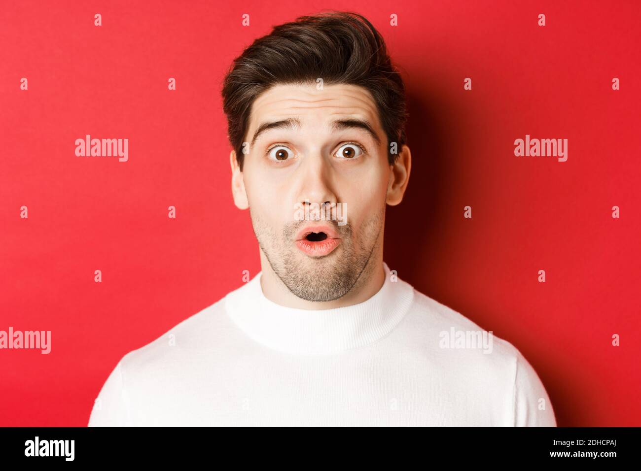 Close-up of surprised handsome man in white sweater, open mouth and ...