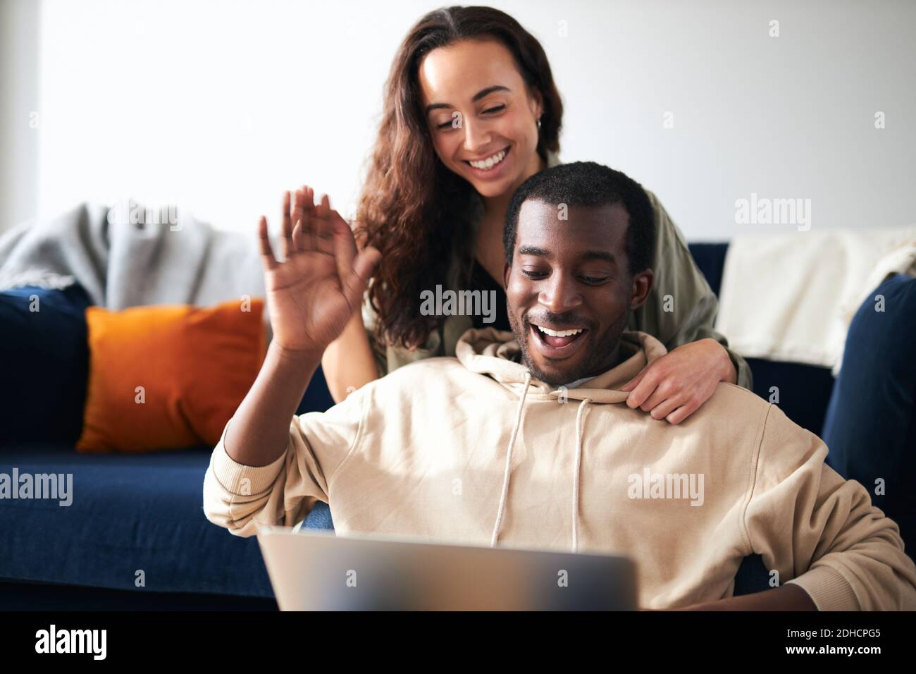 Woman sitting behind man as young mixed ethnicity couple relax on sofa ...