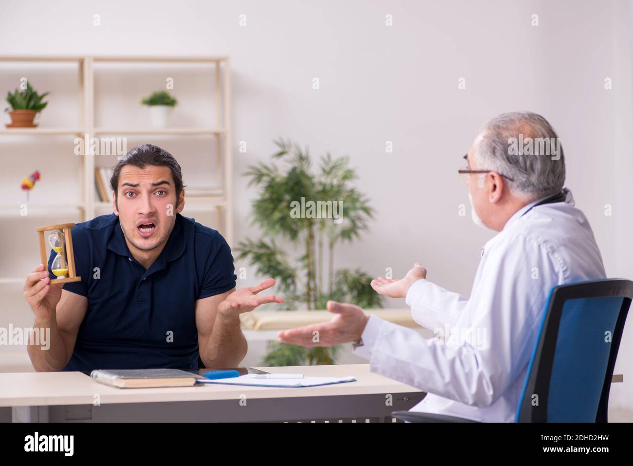 Young male patient visiting old doctor in time management concep Stock ...