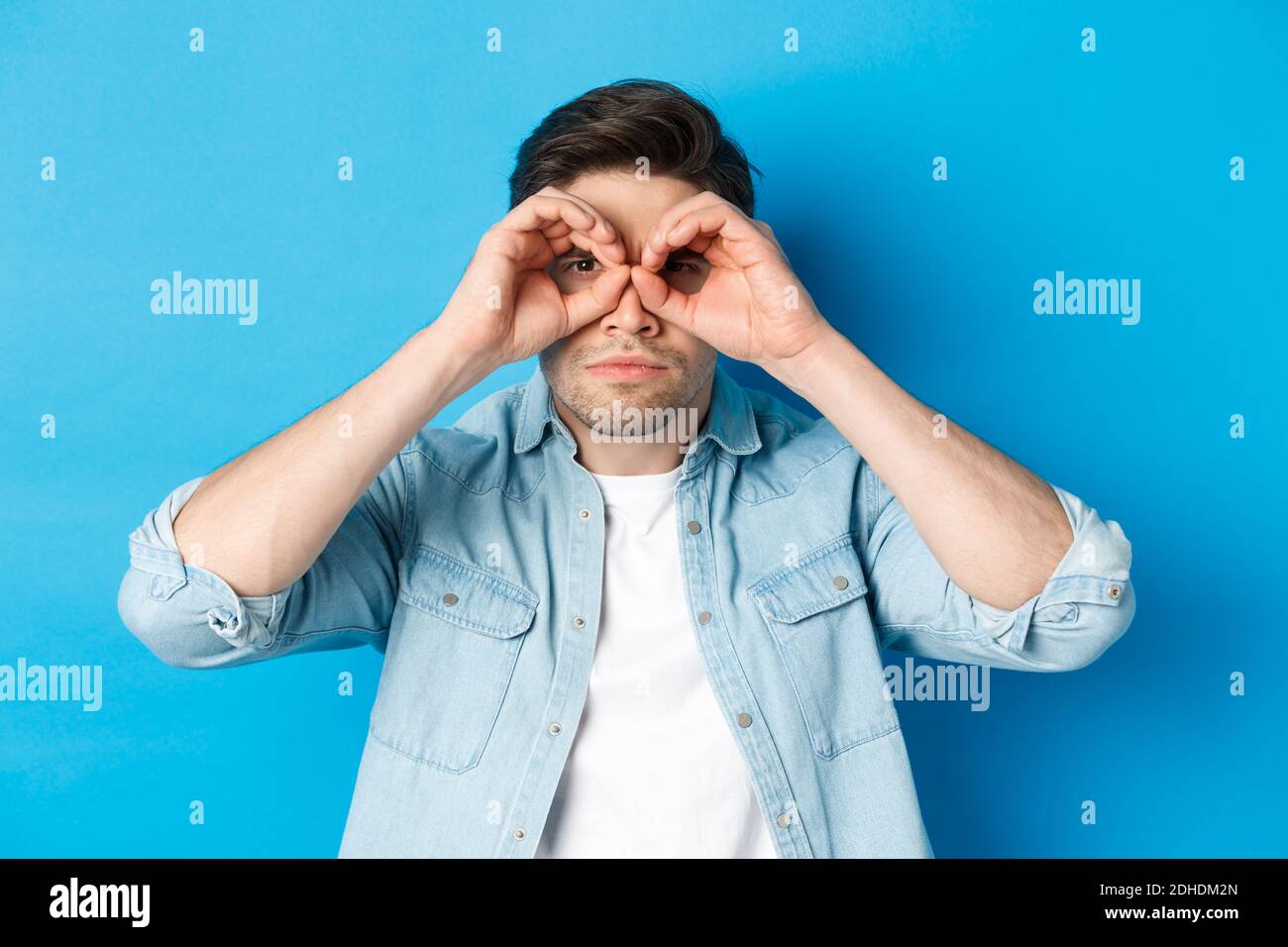 Close-up of man holding hands on eyes, looking through binoculars with ...