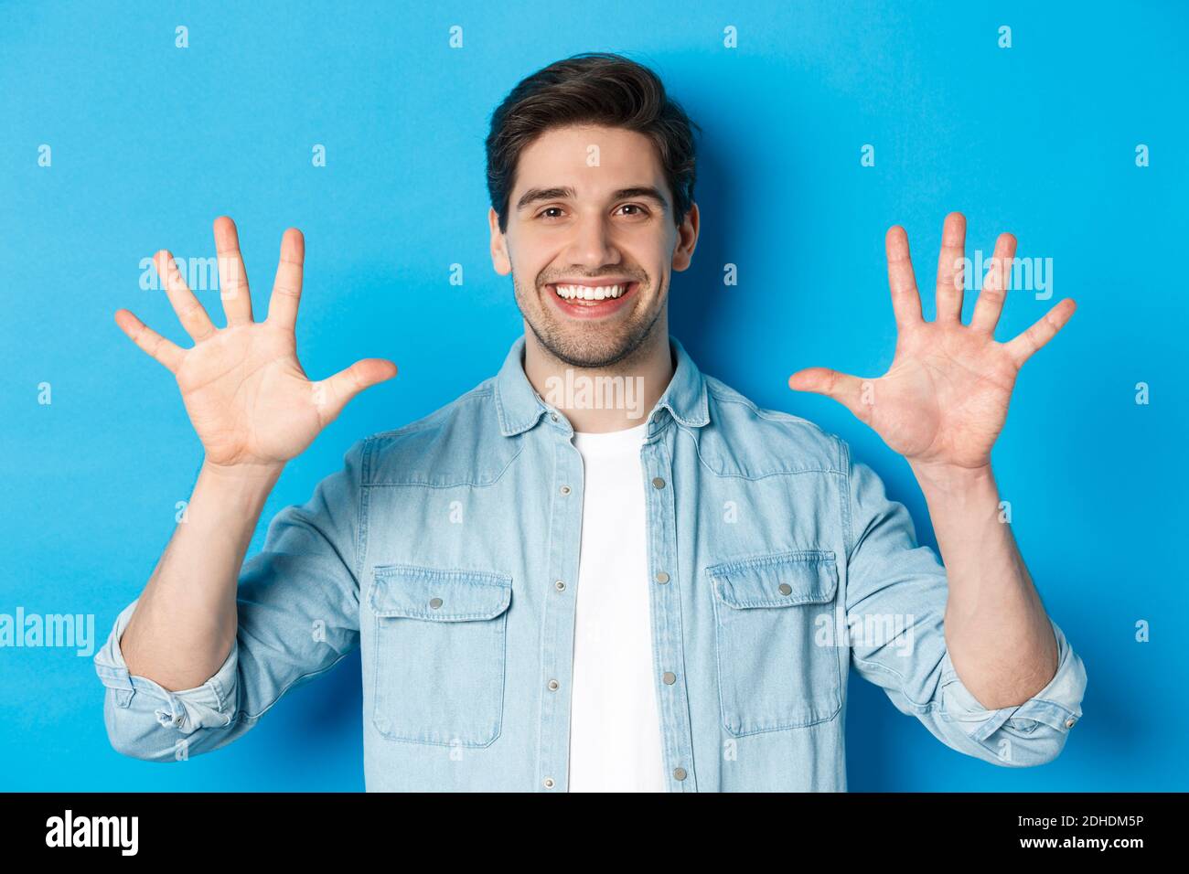 Close-up of handsome man smiling, showing fingers number ten, standing ...
