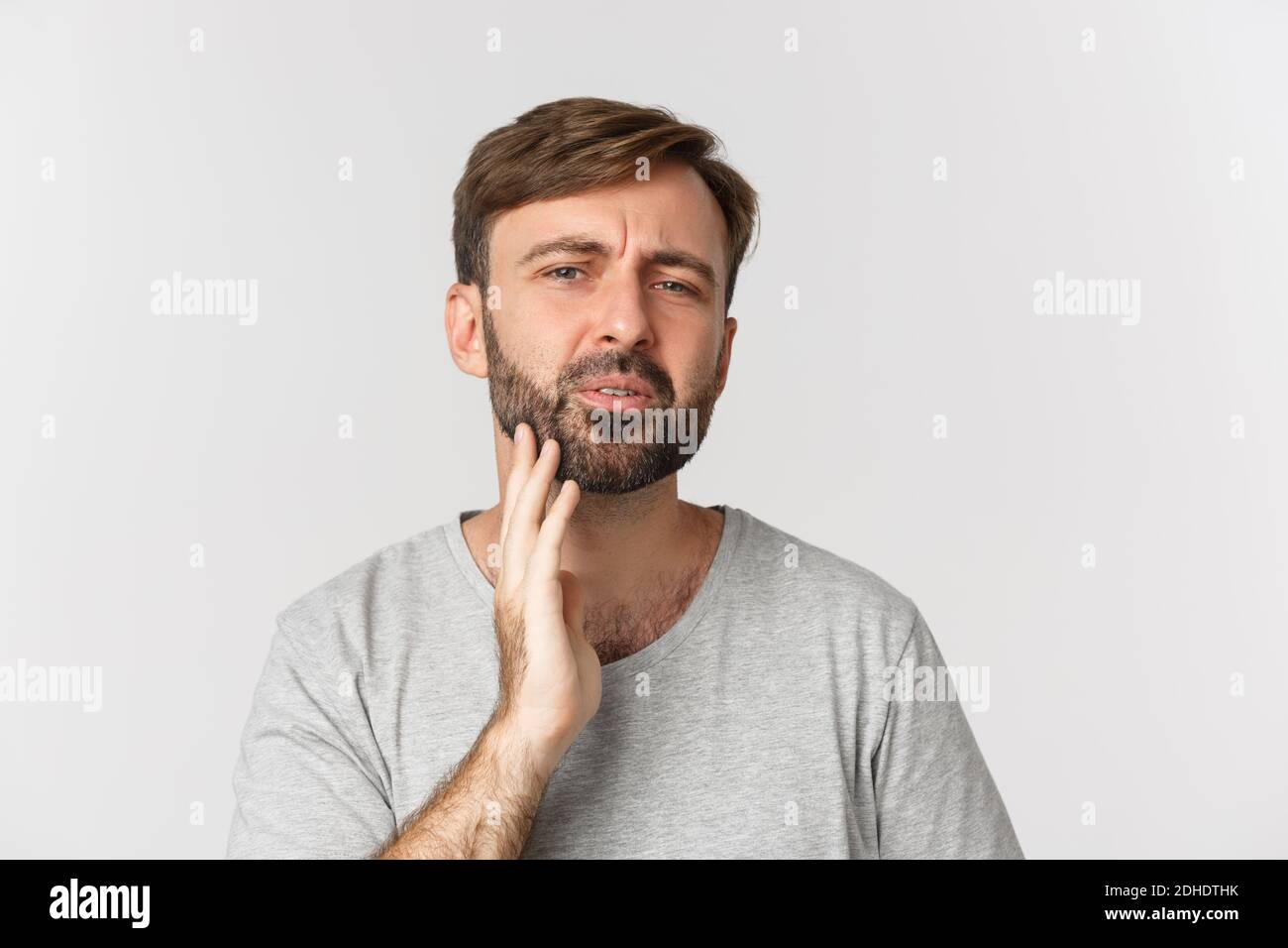 Close-up of confused man touching his beard and looking at himself ...