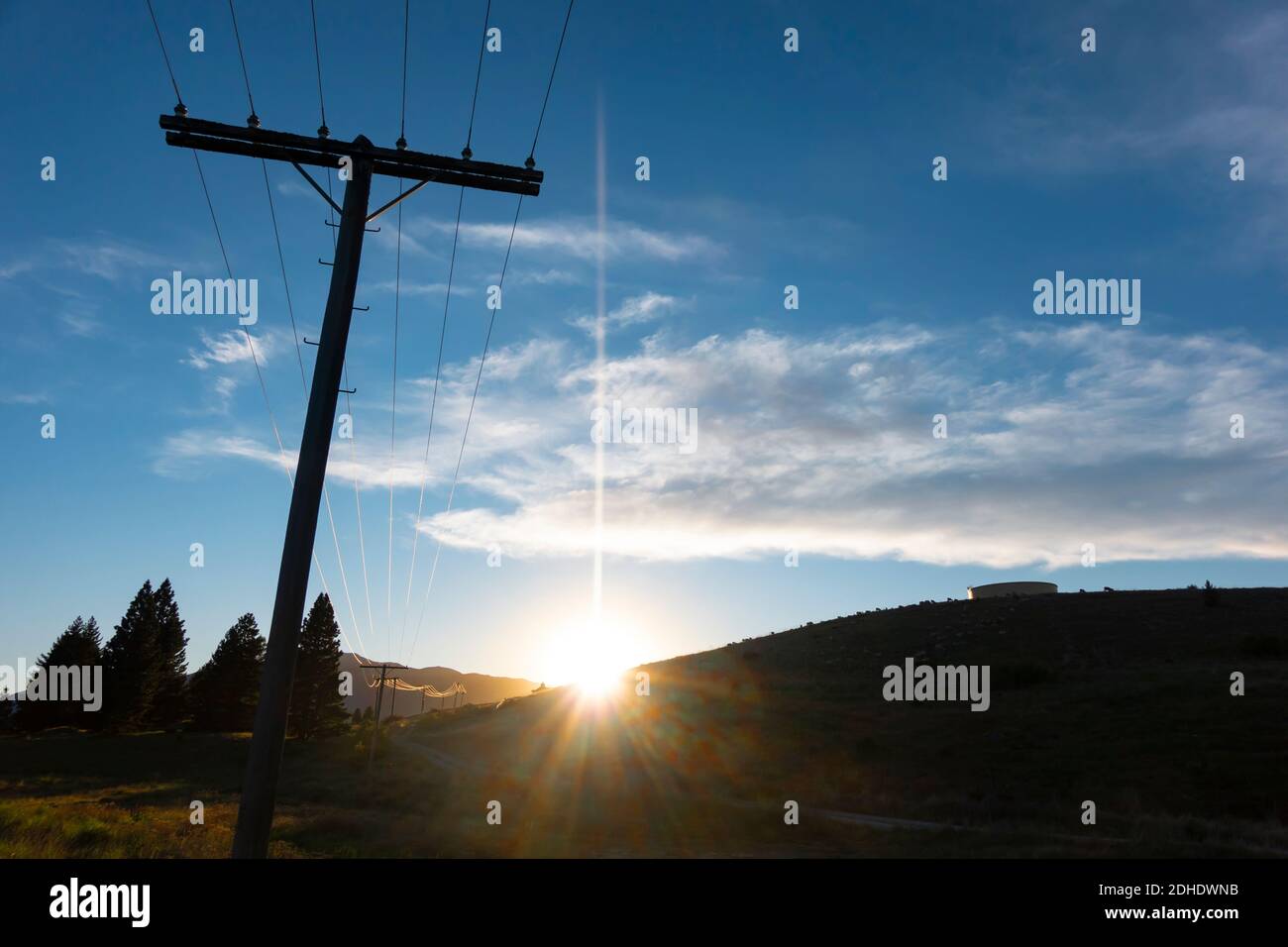 Sun flare through distant hills with power lines glistening in sun and ...
