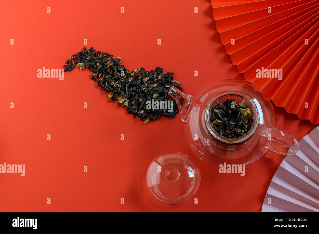 Glass transparent teapot, dry karkade tea leaves. Red background with ...