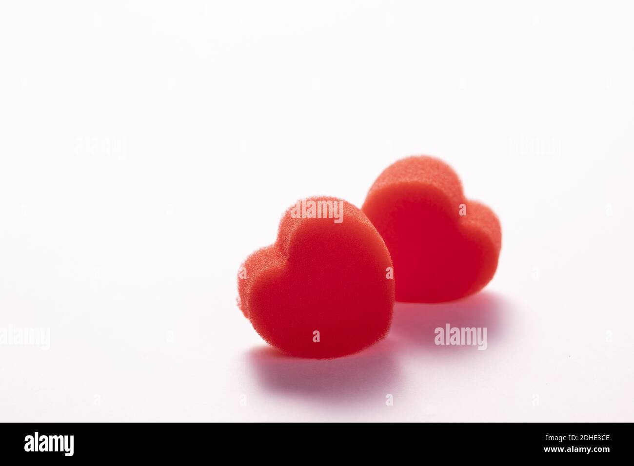 A closeup of two red sponge hearts on a white surface with shadows and ...