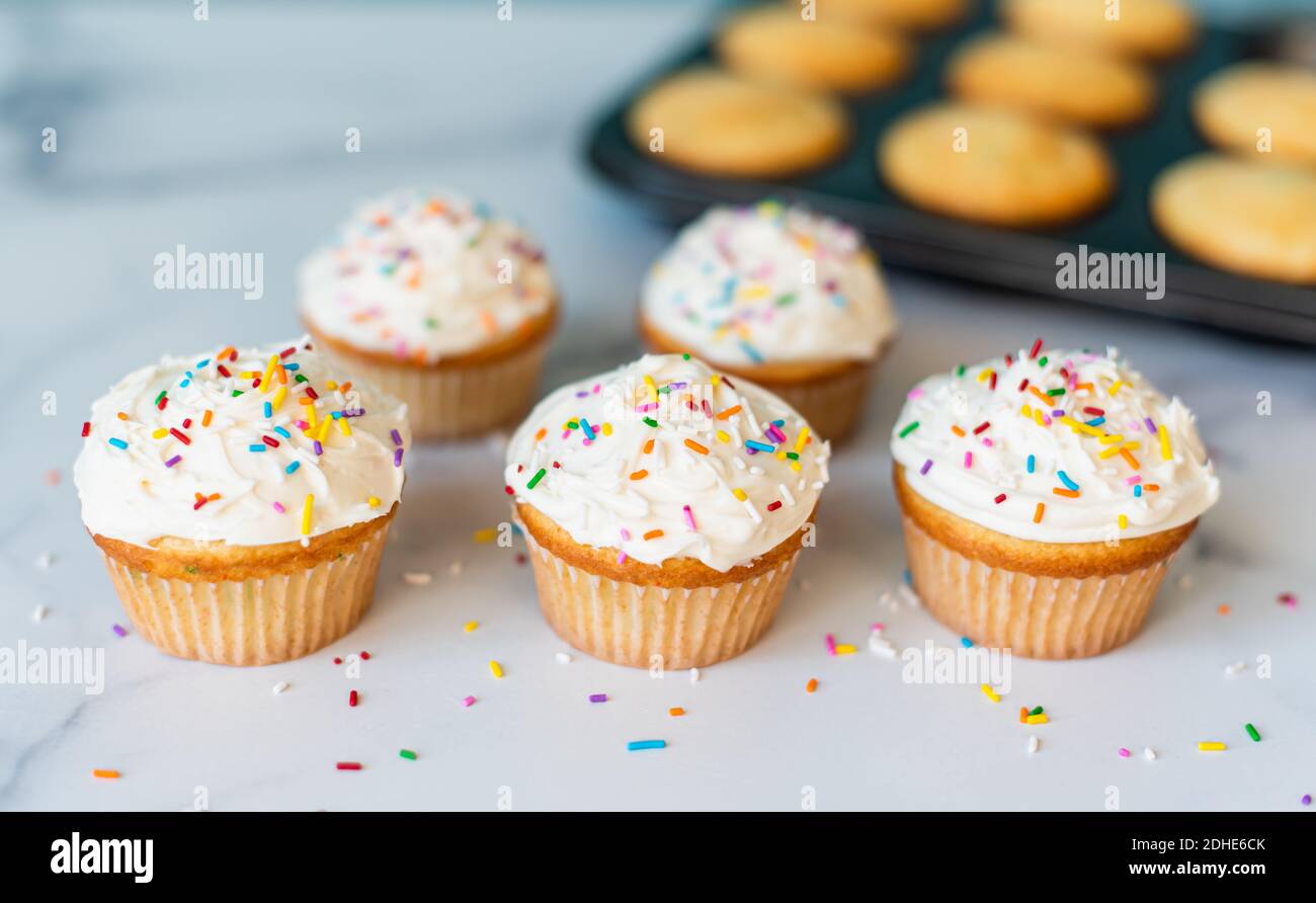 Cupcakes with white frosting and sprinkles on white marble surface ...