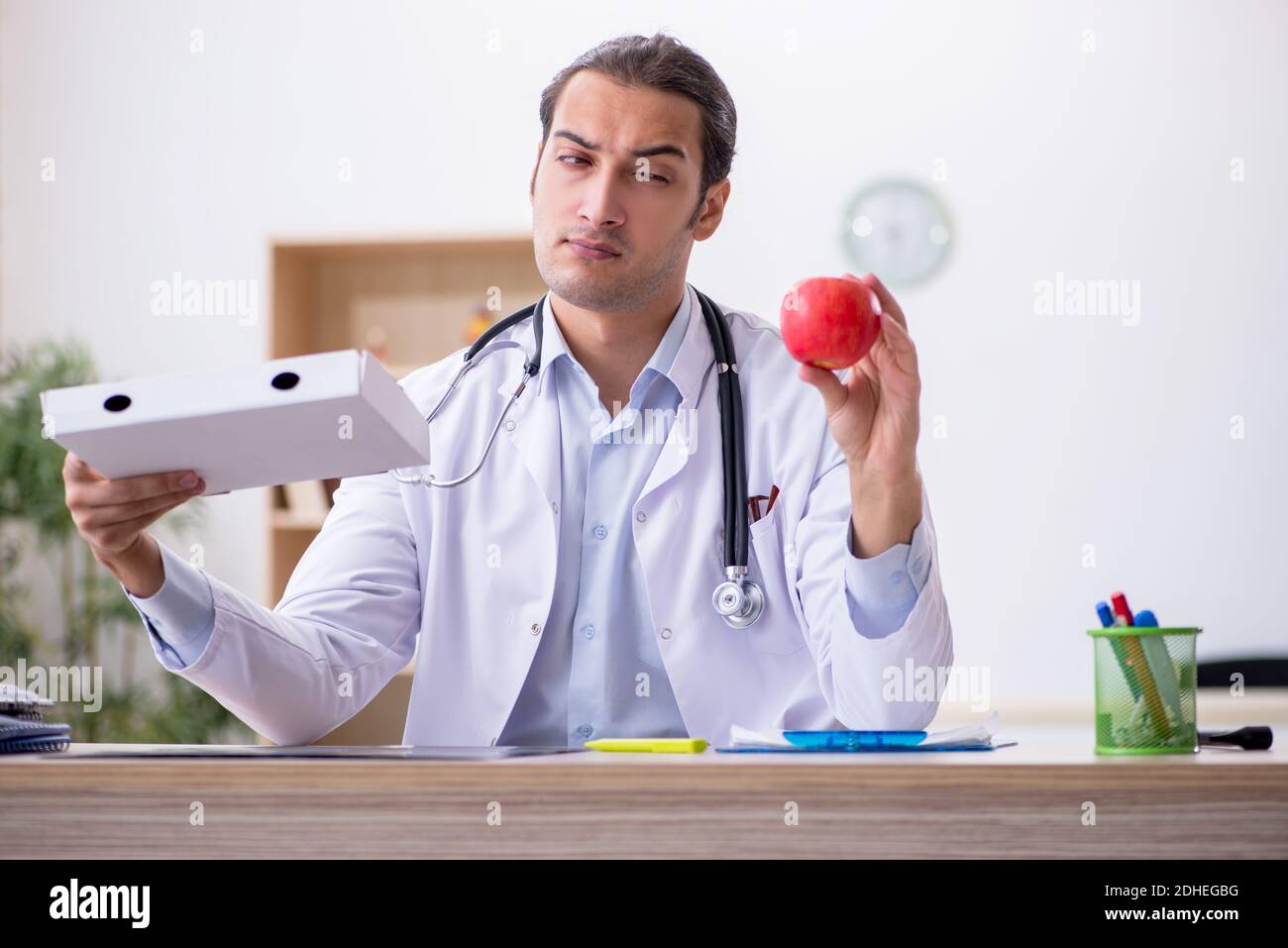 Young male doctor dietician holding apple and pizza box Stock Photo - Alamy