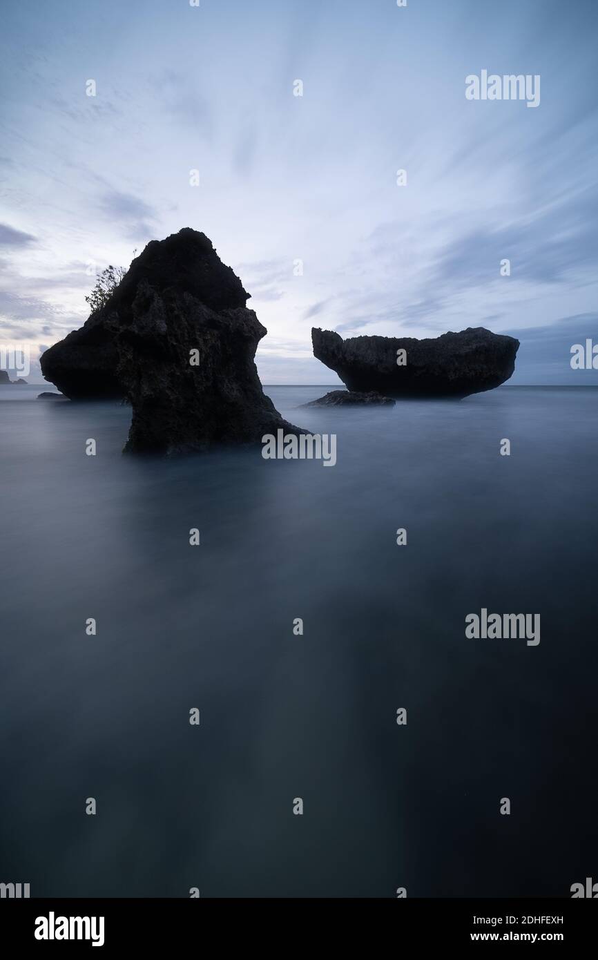 A vertical shot of rocks in a sea on background of the gloomy sky ...