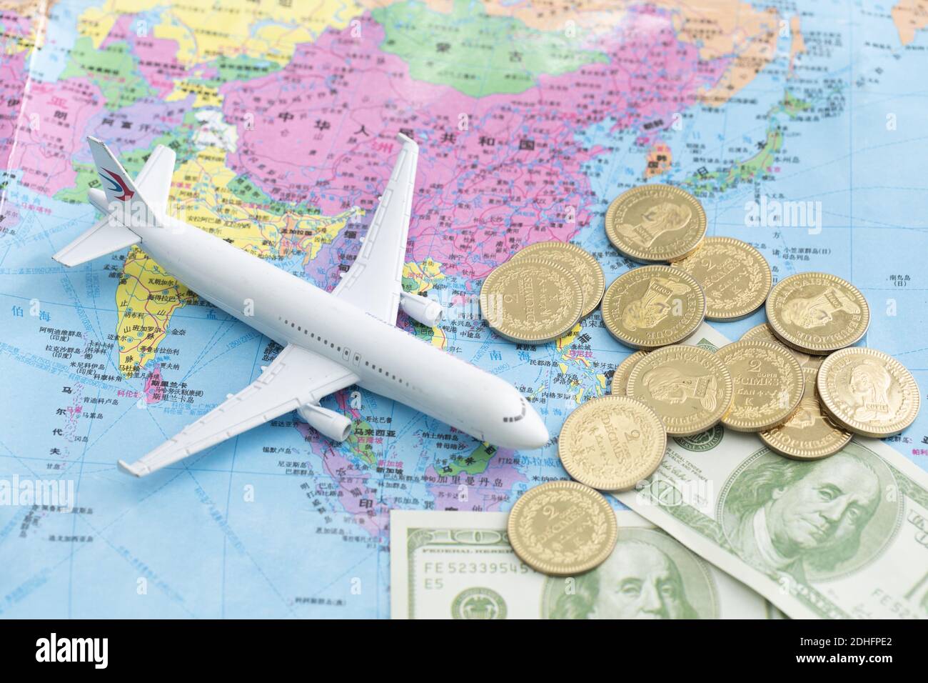 A closeup of a toy airplane, coins, and dollar paper bills on a world ...