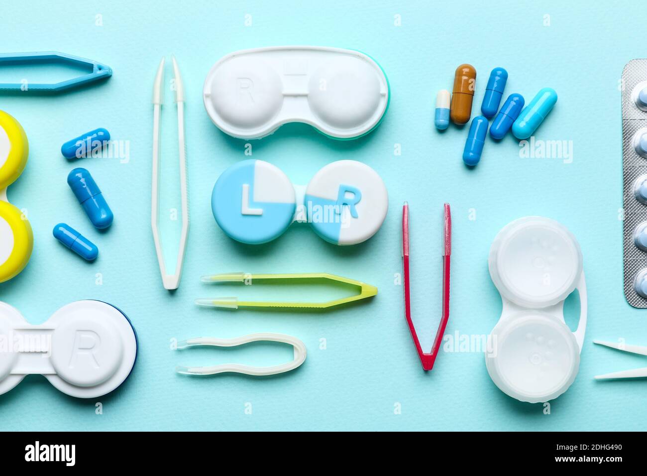 Containers with contact lenses, tweezers and pills on color background ...
