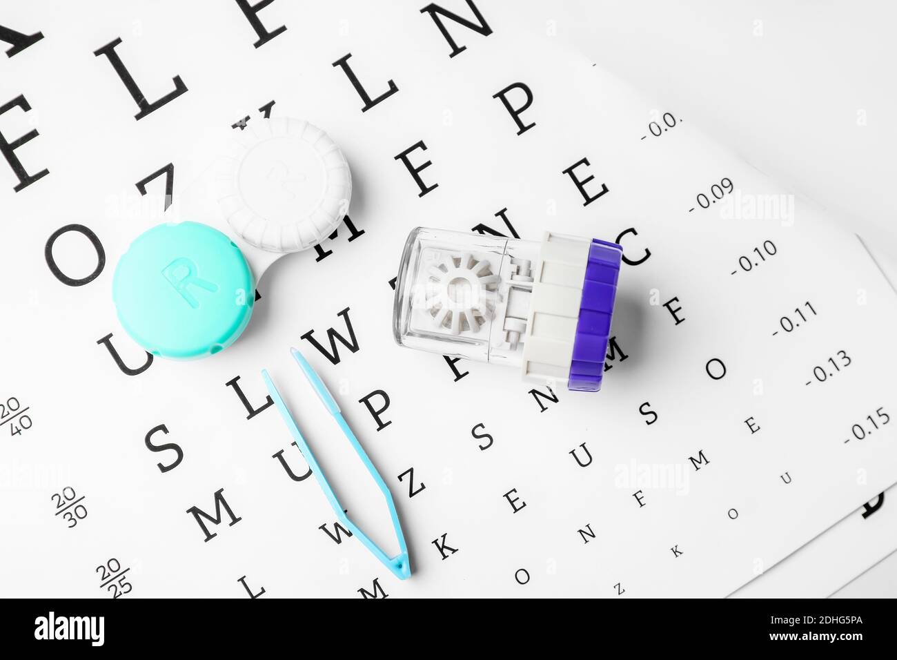 Container with contact lenses, tweezers and eye test chart on white ...