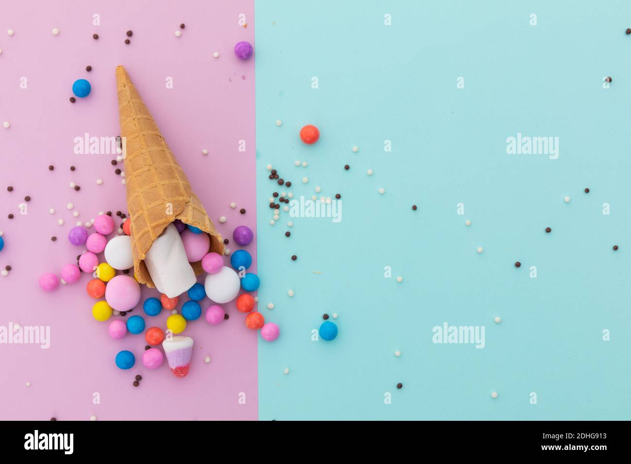 Ice cream cone and scattered colourful sprinkle on pink and blue ...