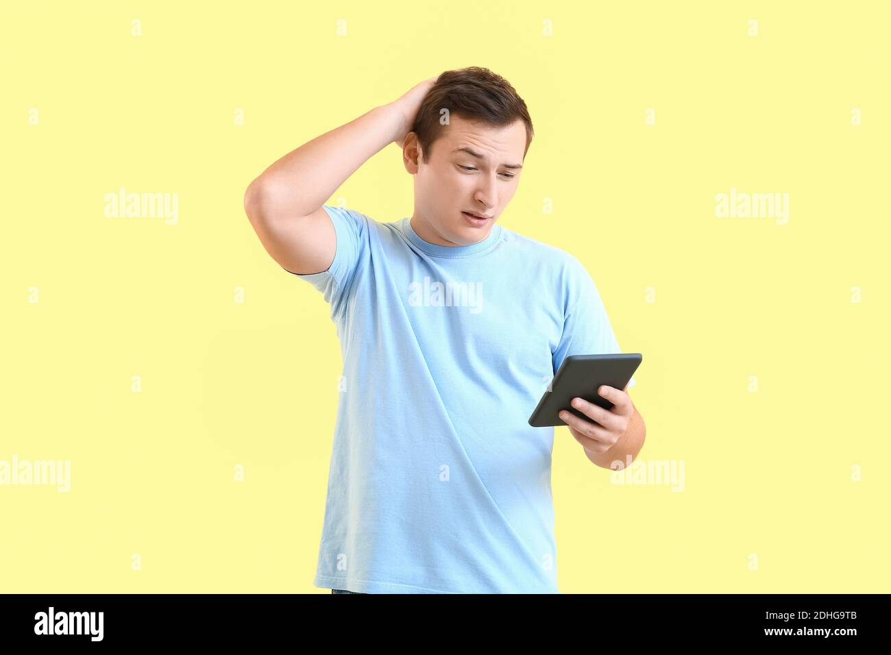 Confused young man with e-reader on color background Stock Photo - Alamy