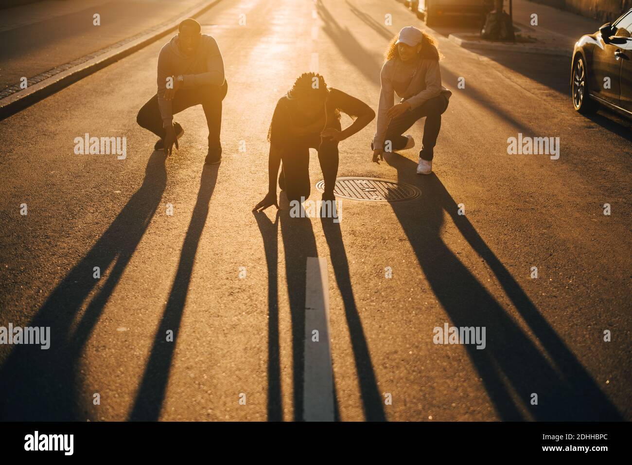 Full length of friends dancing on street in sunlight during sunset ...