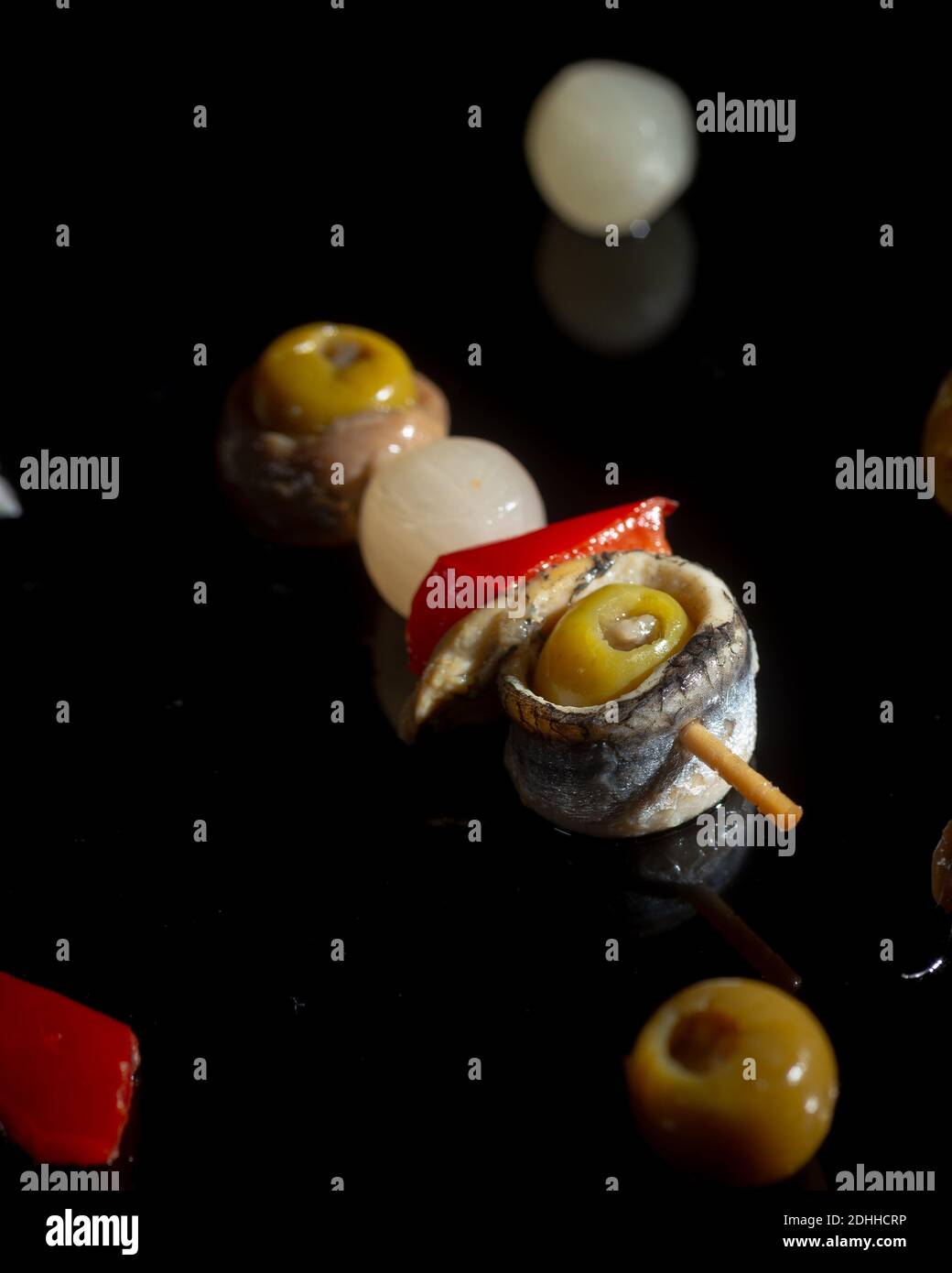 A vertical shot of grilled fish with green olives in a stick on a black ...