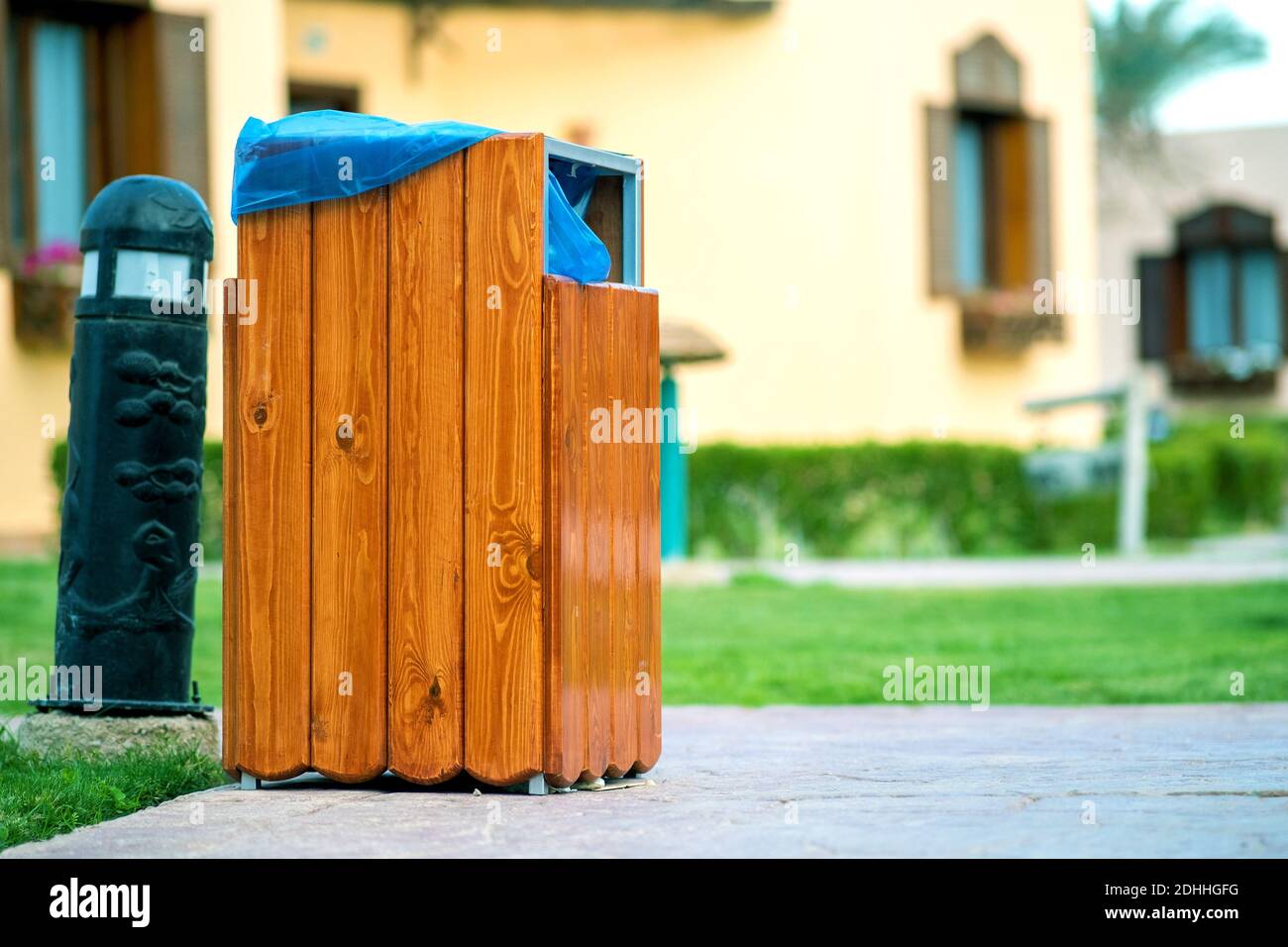 Yellow wooden trash can outdoors on the side of sidewalk in park ...