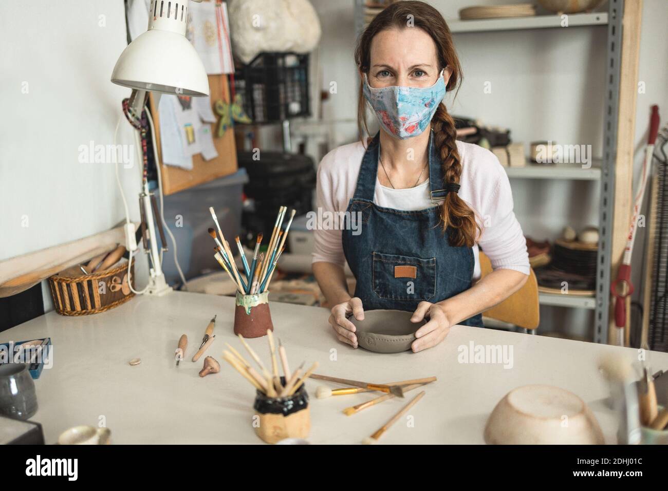 Caucasian woman making ceramic soup plate while wearing protective face ...