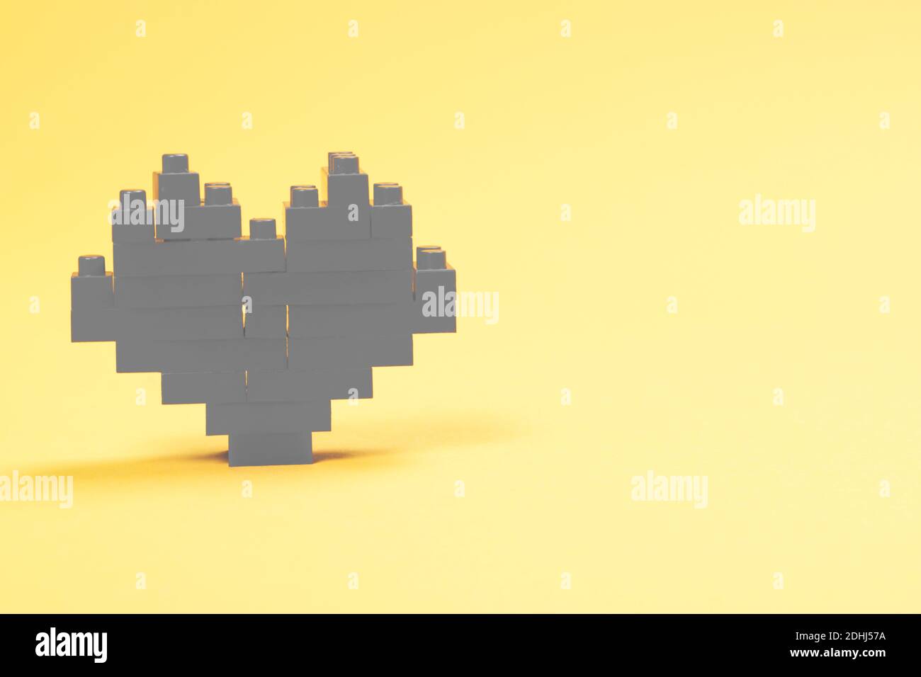 Gray heart made of plastic constructor blocks on yellow background ...