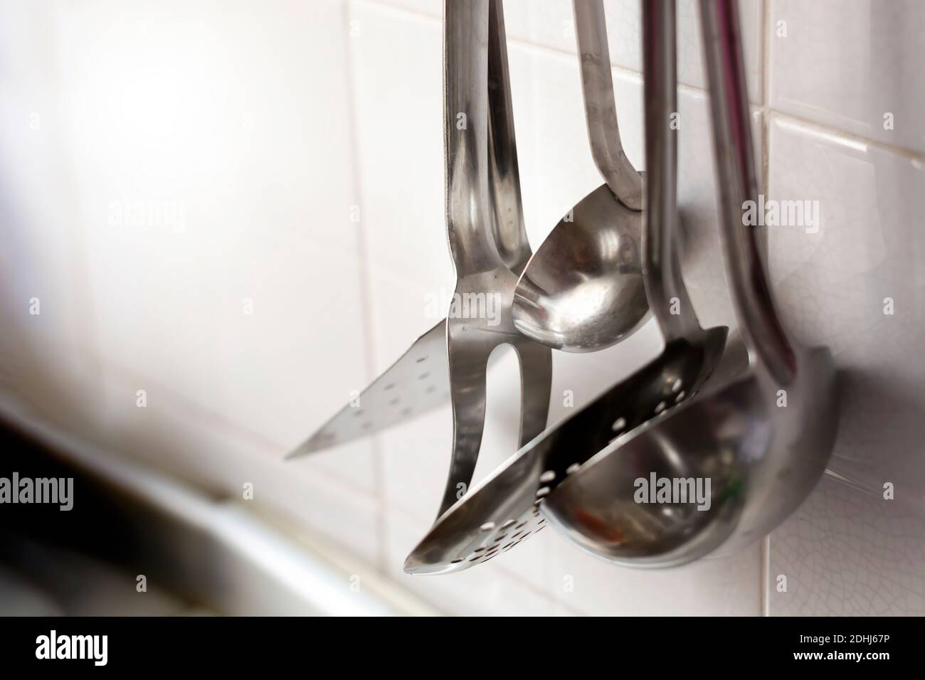 A skimmer, two forks and two metal ladles hanging on the tiled kitchen ...