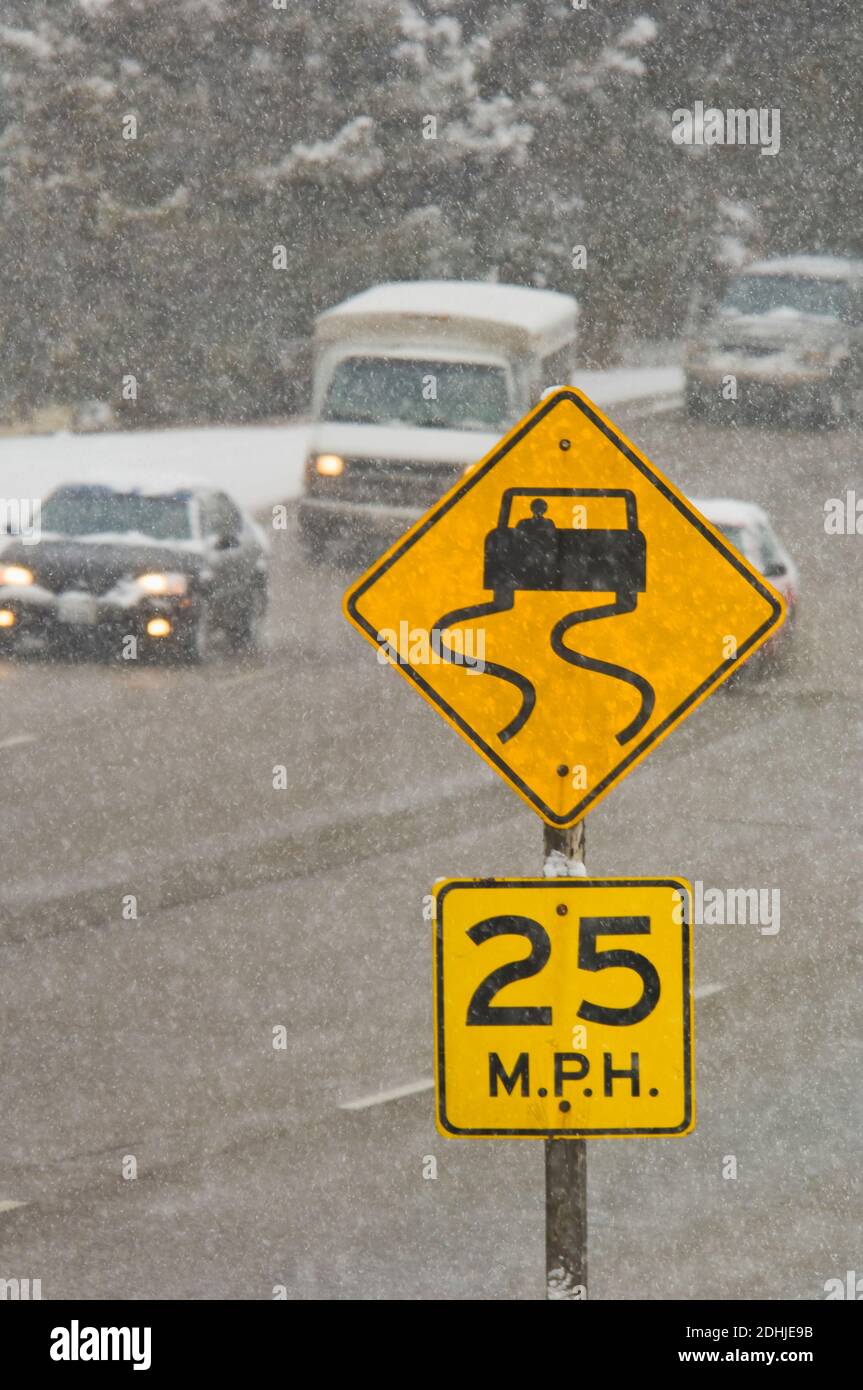 Traffic driving on snowy road with road sign warning of skid danger ...