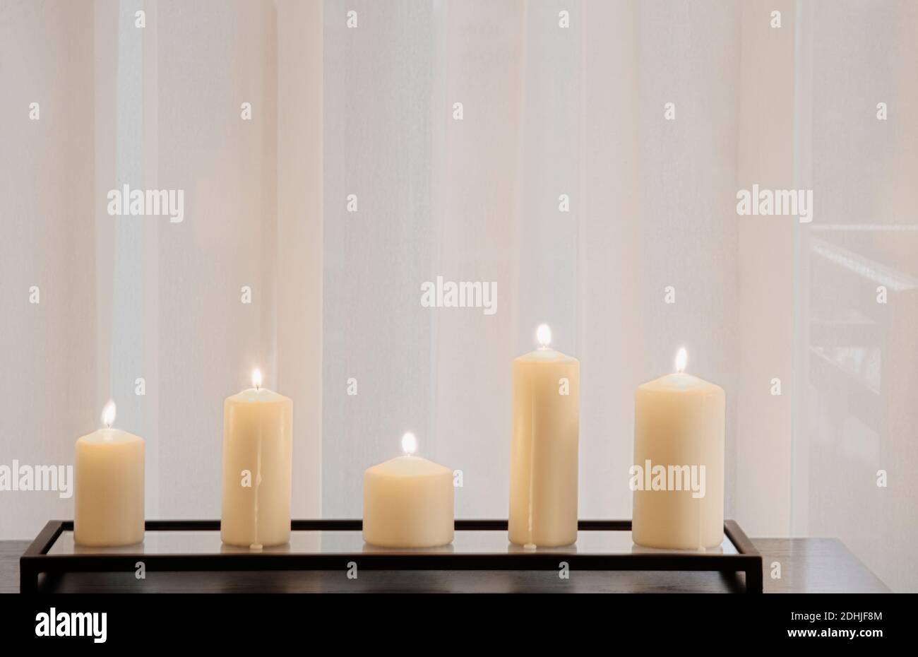 Pillar candles lit and lined up in front of curtain Stock Photo - Alamy