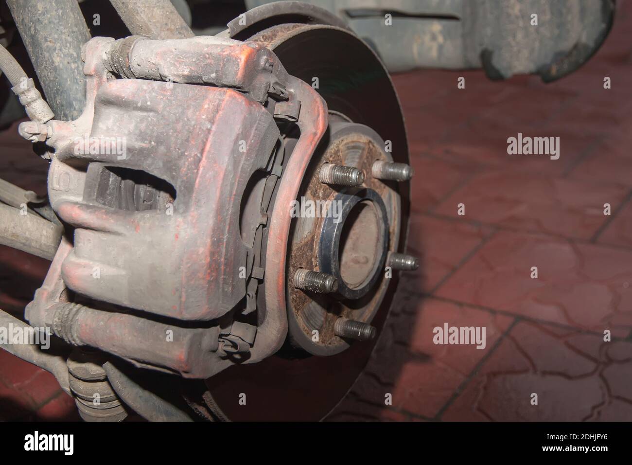 Rusty front hub of a car wheel with a brake disc and a red caliper. A ...