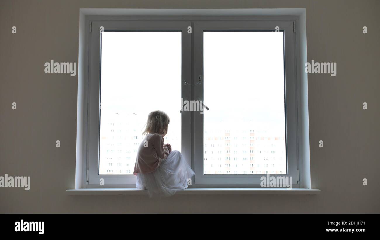 Lonely child girl sitting on the windowsill at the window in the ...