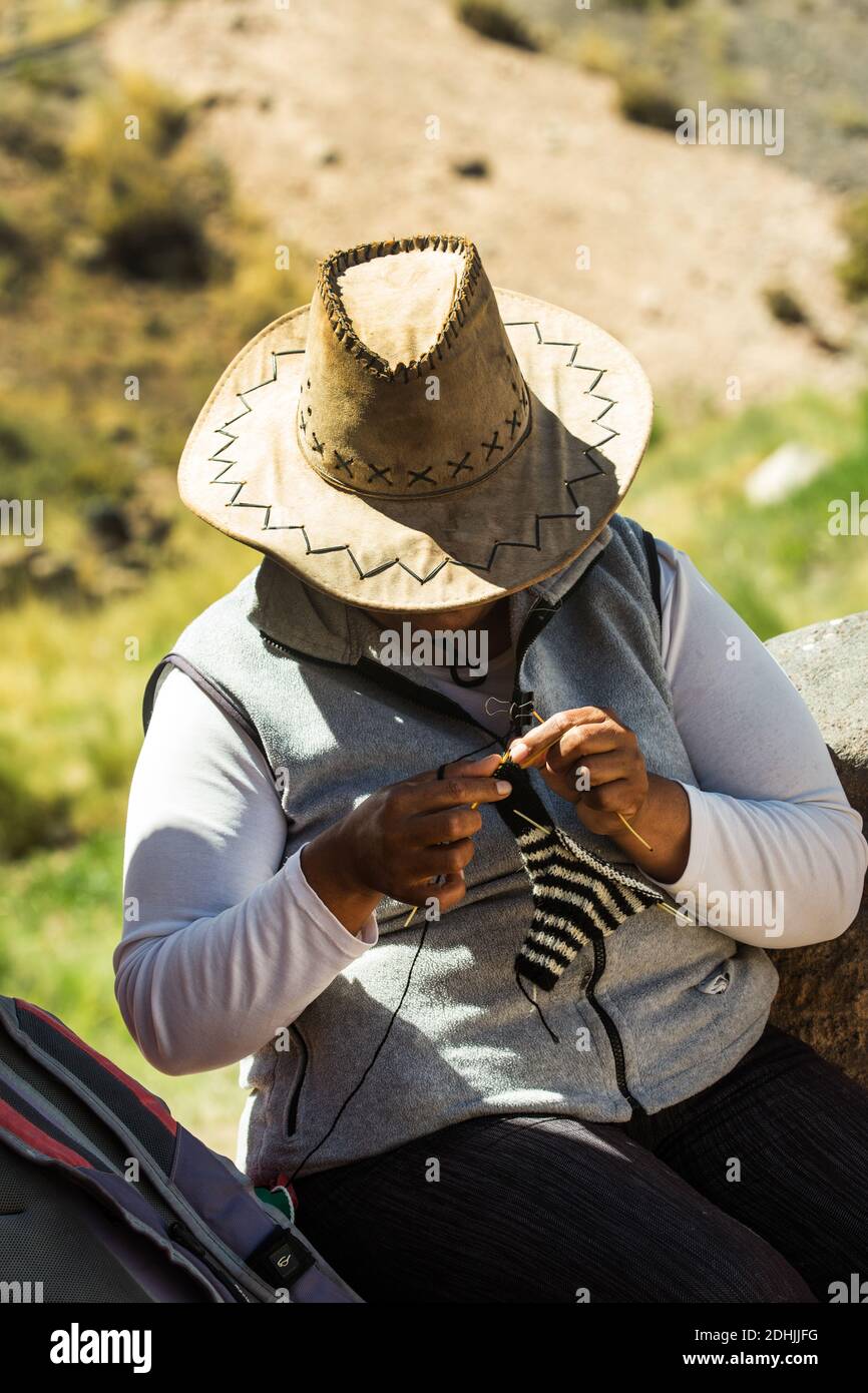 An indigenous Indian woman sits knitting in the shade, wearing a grass ...