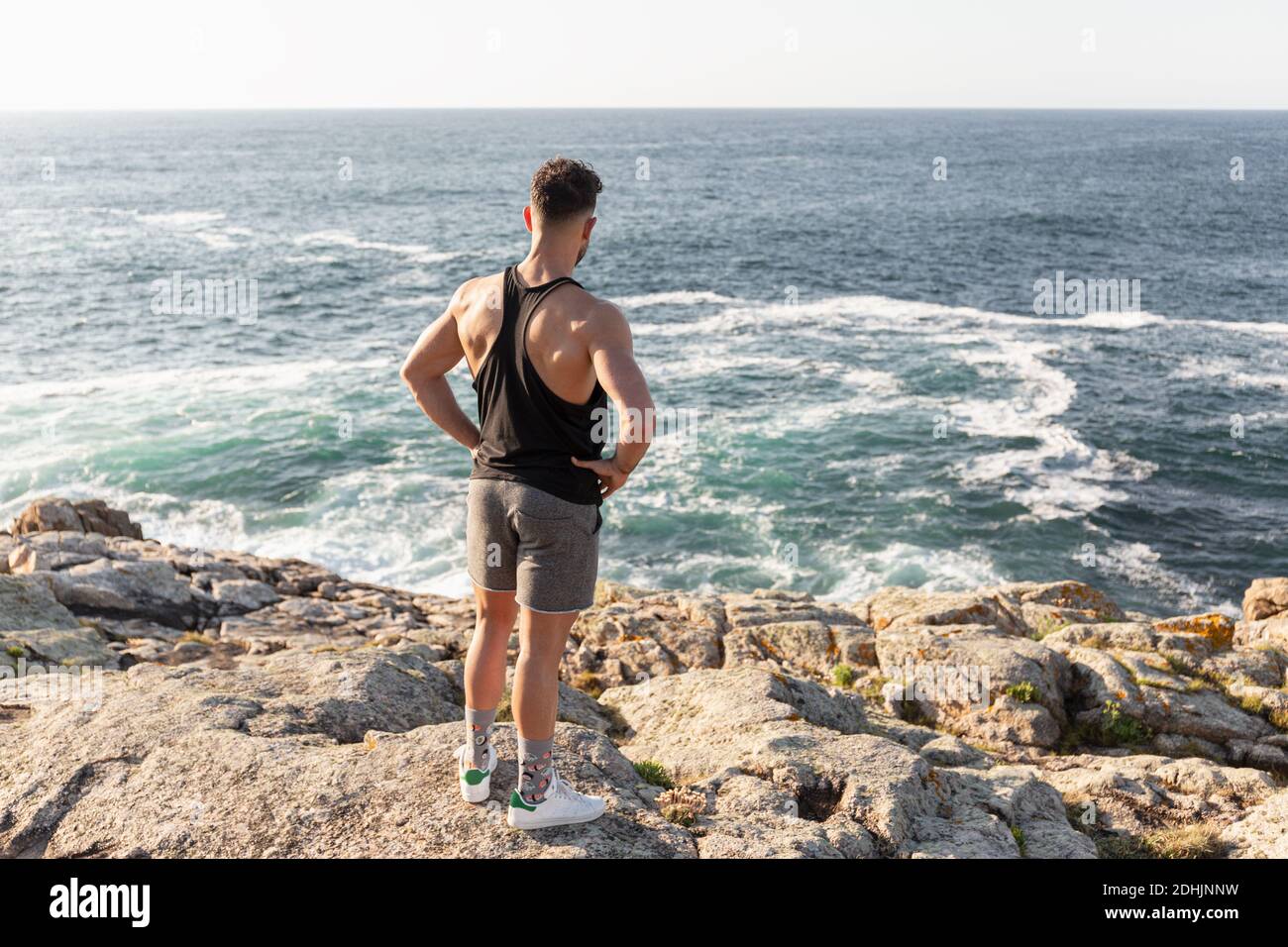 Back view of muscular male athlete in sportswear standing on beach and ...