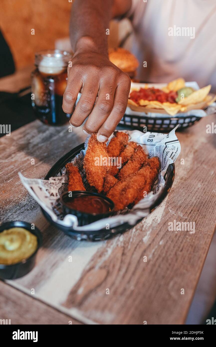 Crop anonymous black African male eating delicious chicken wing with ...