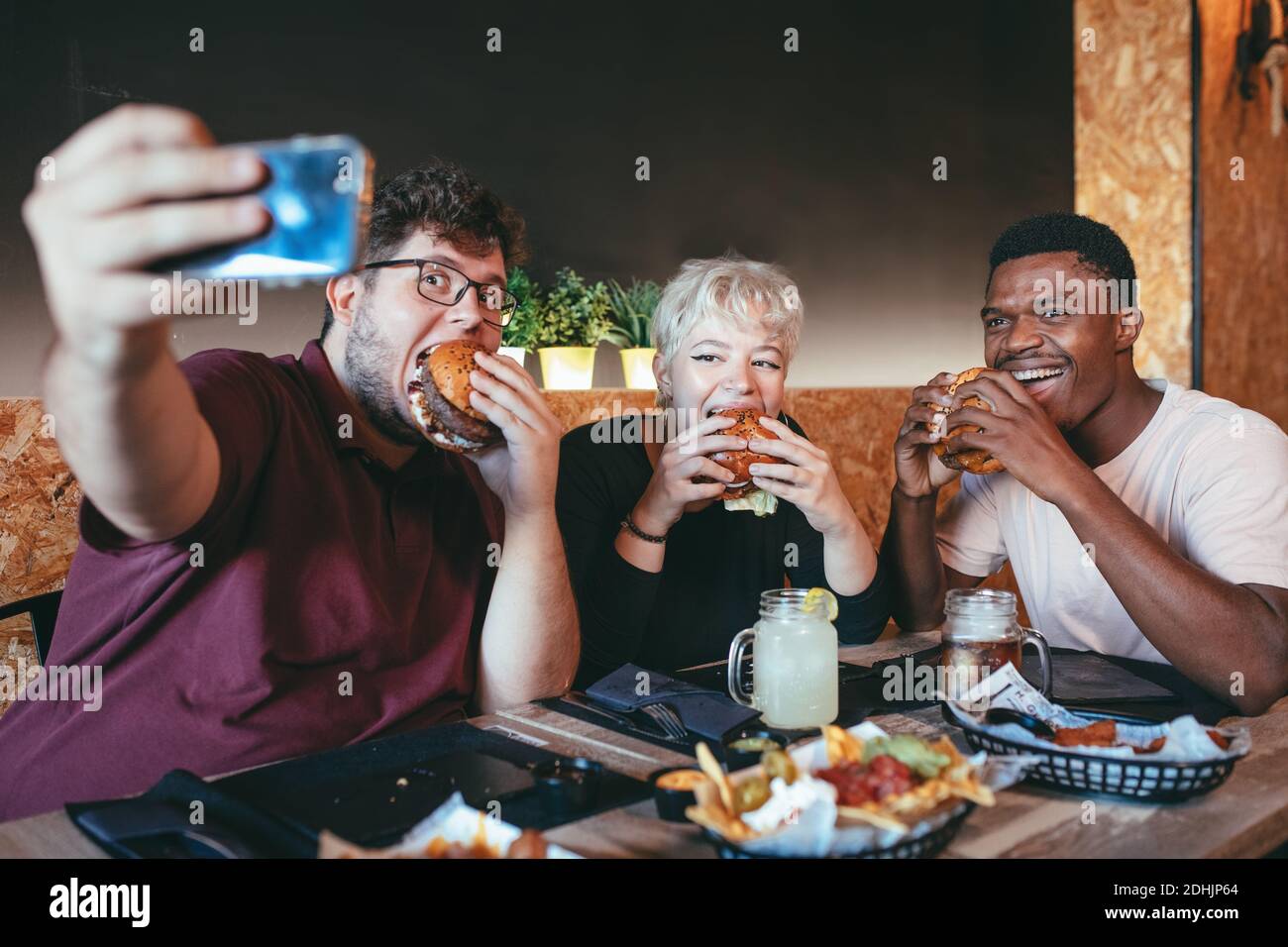 Cheerful multiethnic friends eating burgers in fast food cafe and ...