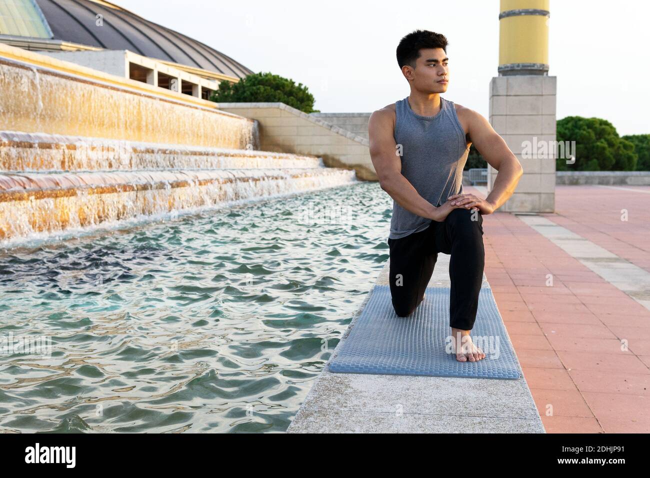 Peaceful Asian male standing barefoot on mat in Anjaneyasana on knee ...