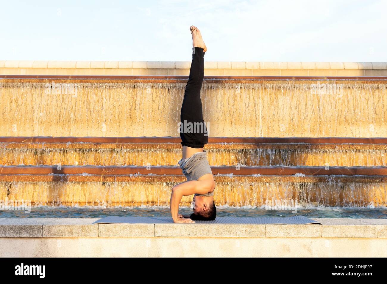 Side view of slim male standing in Supported Headstand pose on mat and ...
