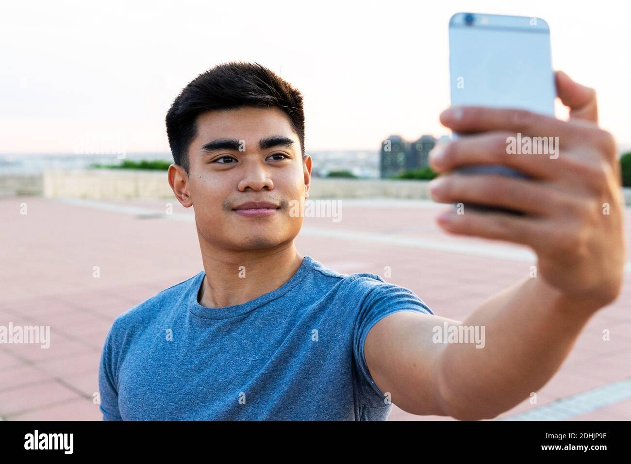 Handsome Asian male standing in city while taking photo on selfie ...
