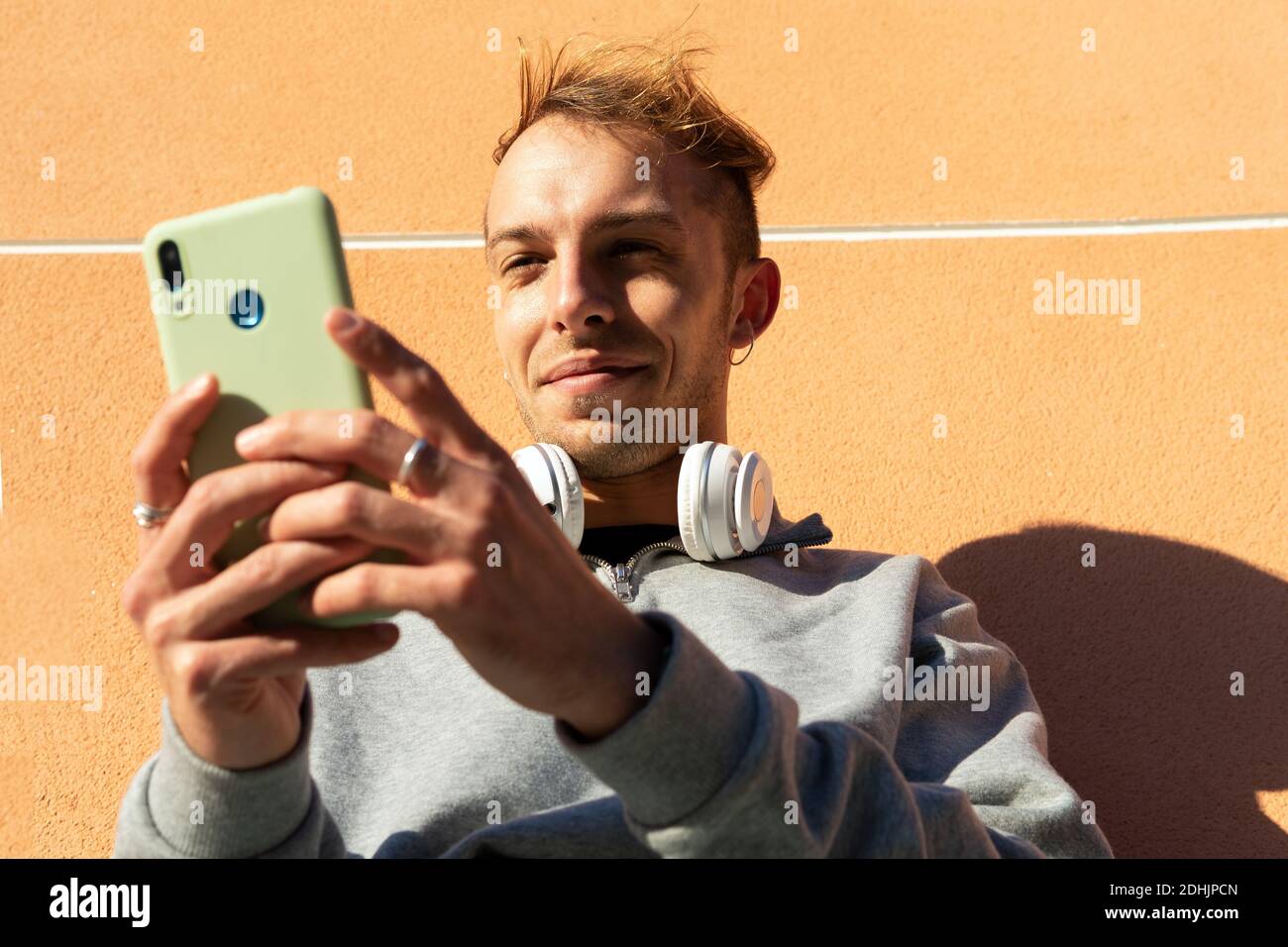 Low angle of positive young guy in casual outfit with headphones on ...