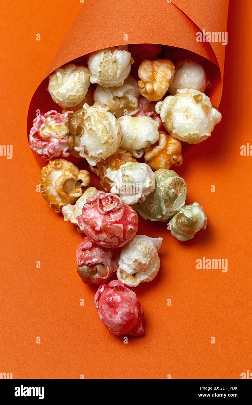 High angle of colorful tasty popcorn in paper cone placed on orange ...