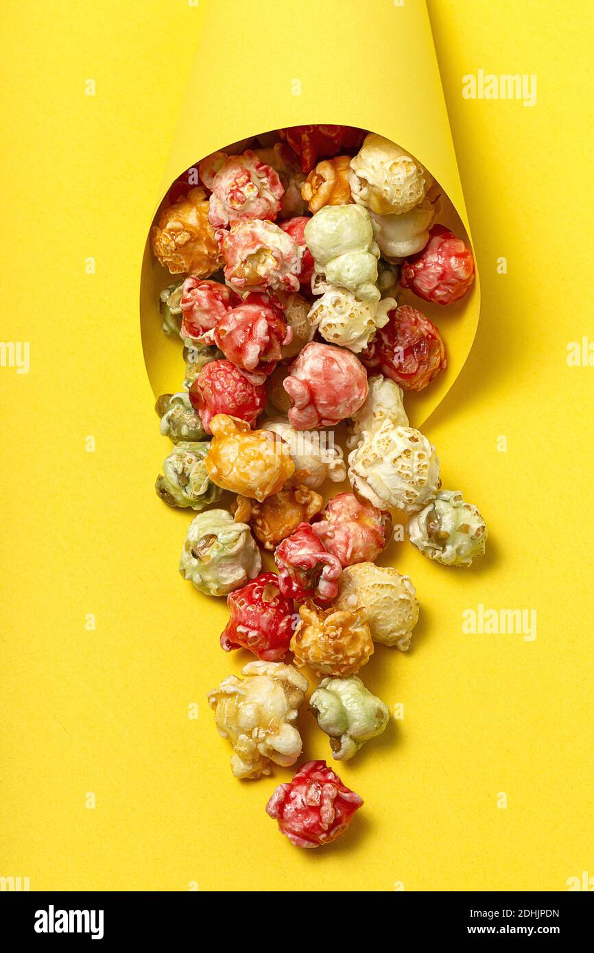 High angle of colorful tasty popcorn in paper cone placed on yellow ...