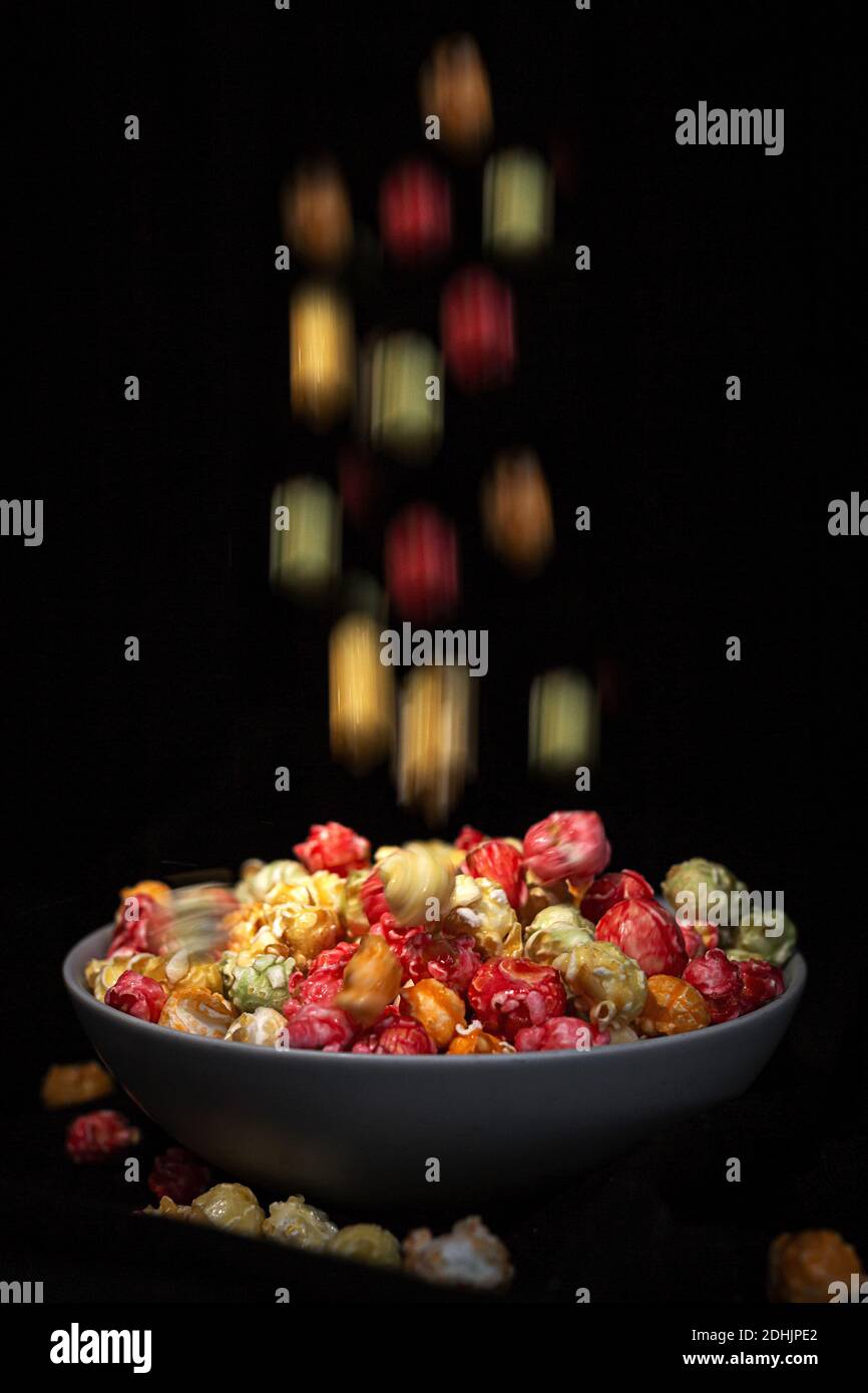 Tasty colorful popcorn falling on heap in bowl placed on black ...