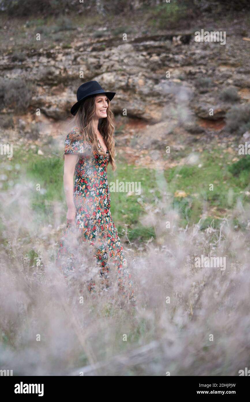 Side view of gentle female in long dress walking in spring park among ...