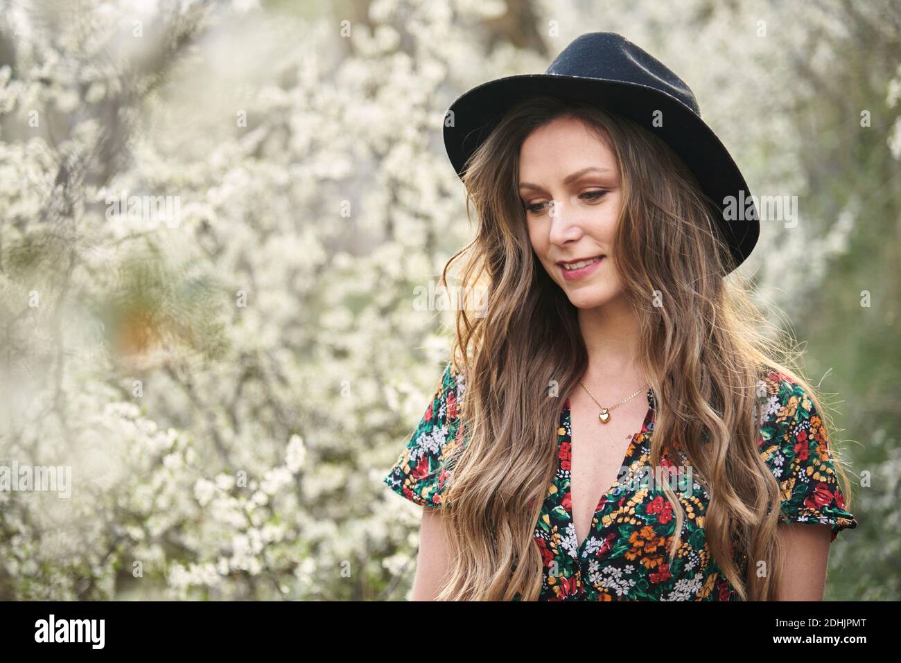 Gentle female in long dress walking in spring park among blooming trees ...