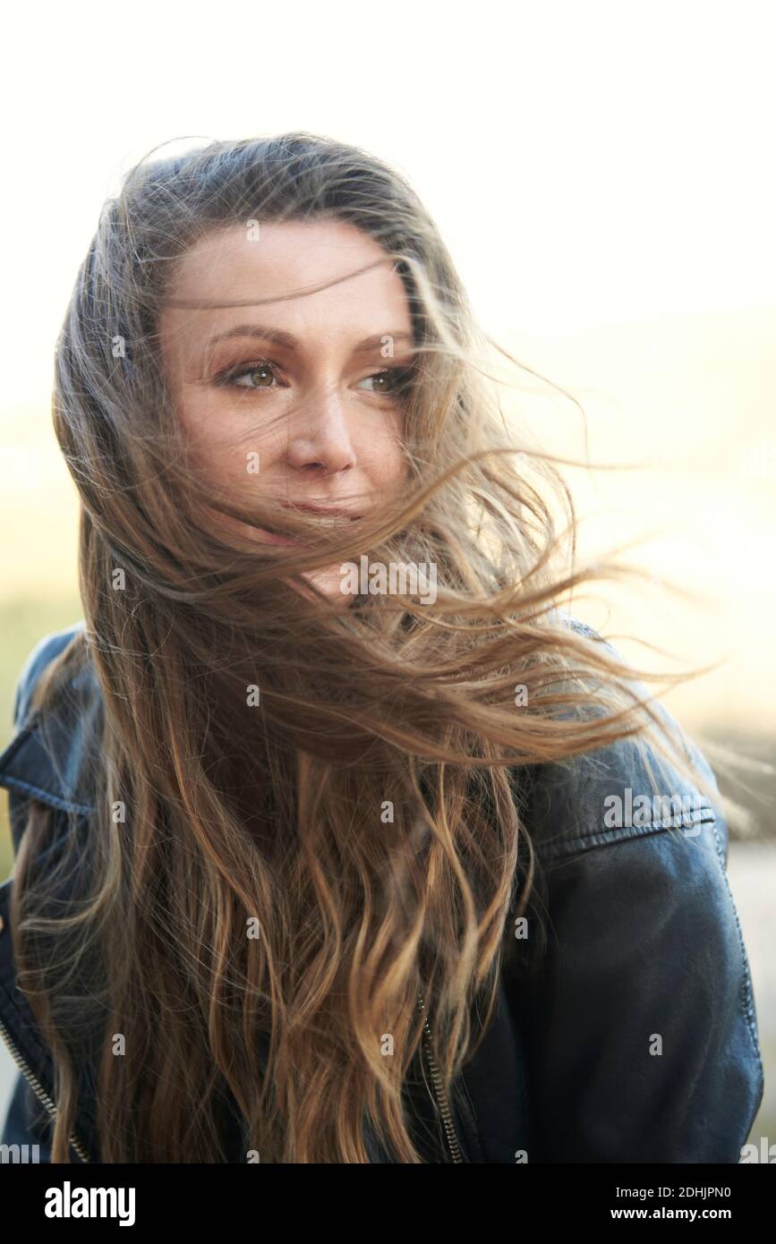 Tranquil female in leather jacket and with long wavy hair standing in ...